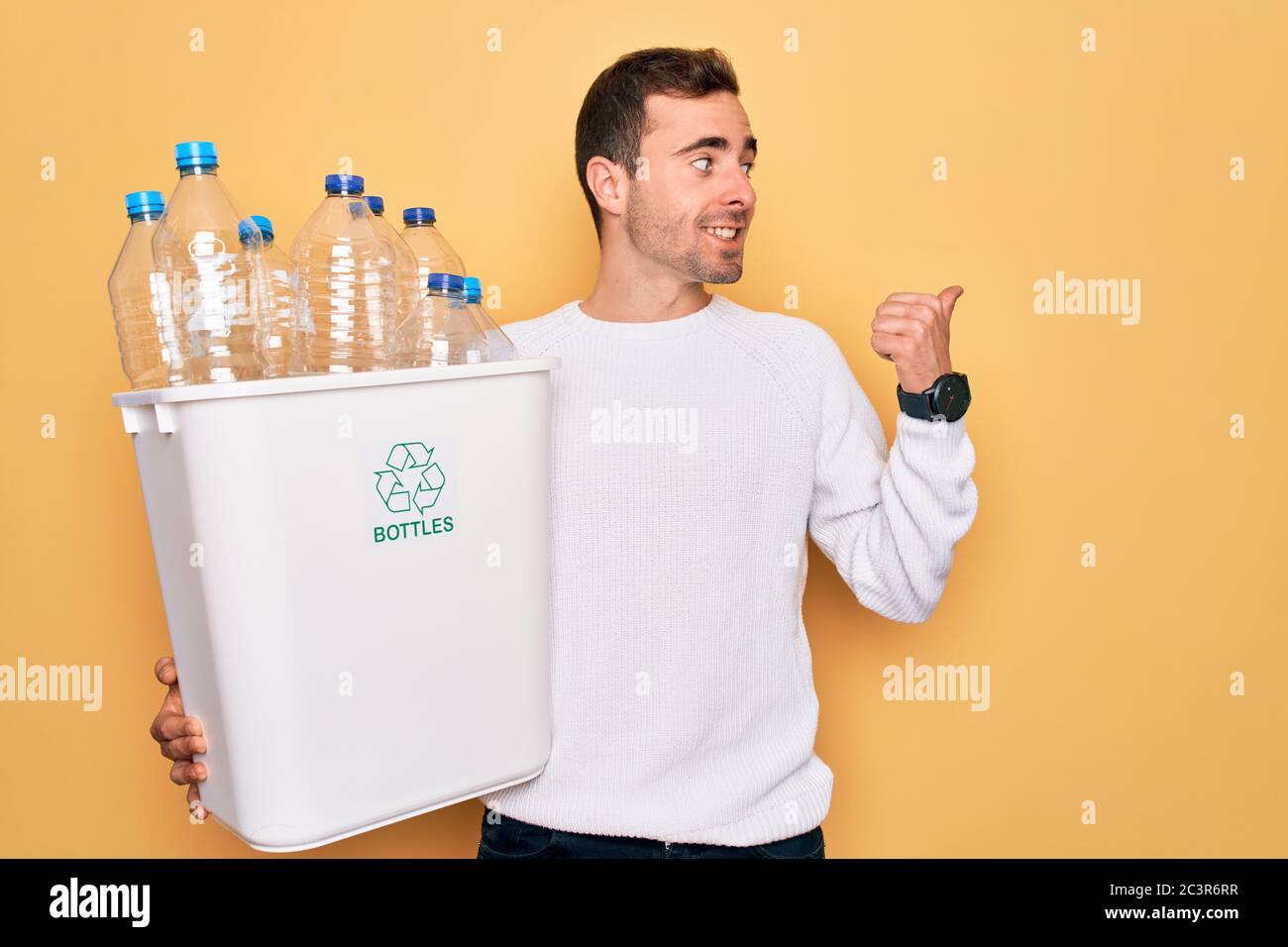 Young handsome man with blue eyes recycling holding wastebasket with ...