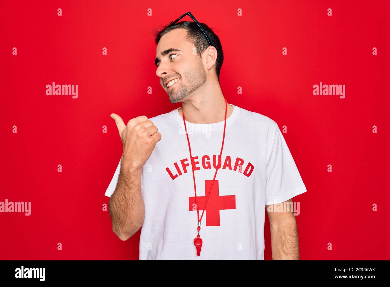 Handsome lifeguard man wearing t-shirt with red cross and whistle over ...