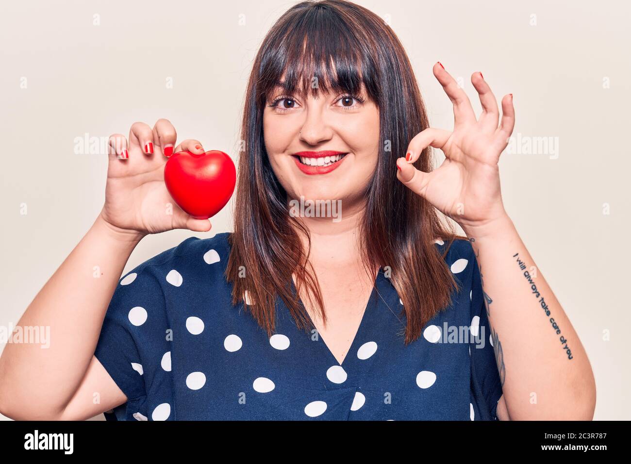 Young plus size woman holding heart doing ok sign with fingers, smiling ...