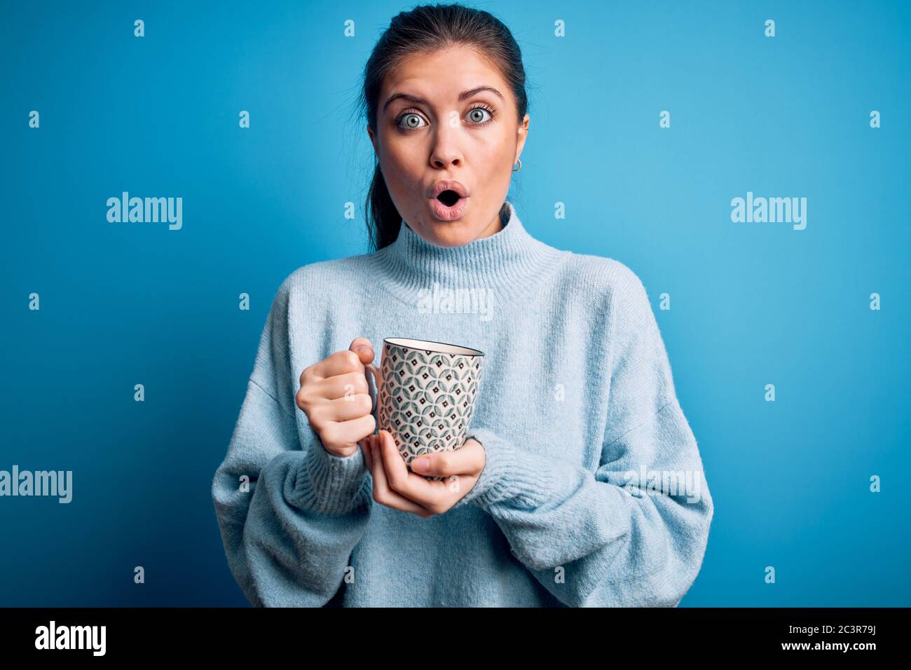 Young beautiful woman with blue eyes drinking mug of coffee over ...