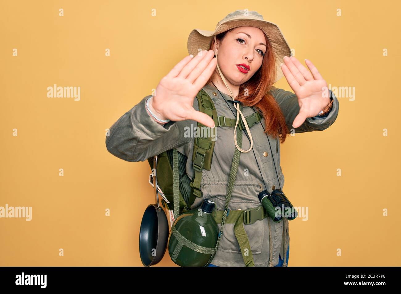 Young redhead backpacker woman hiking wearing backpack and hat over ...