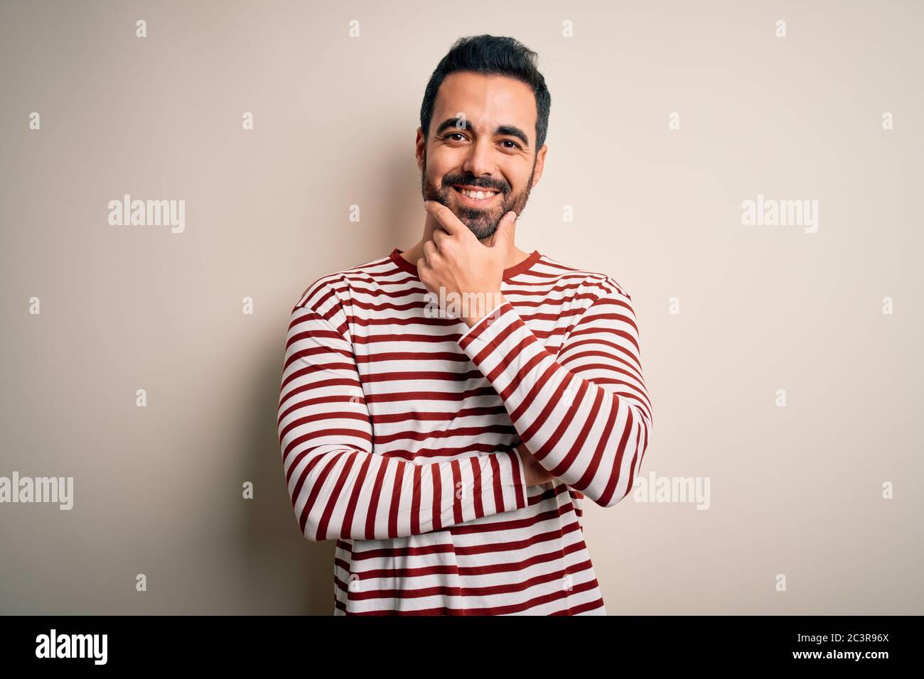 Young handsome man with beard wearing casual striped t-shirt standing ...