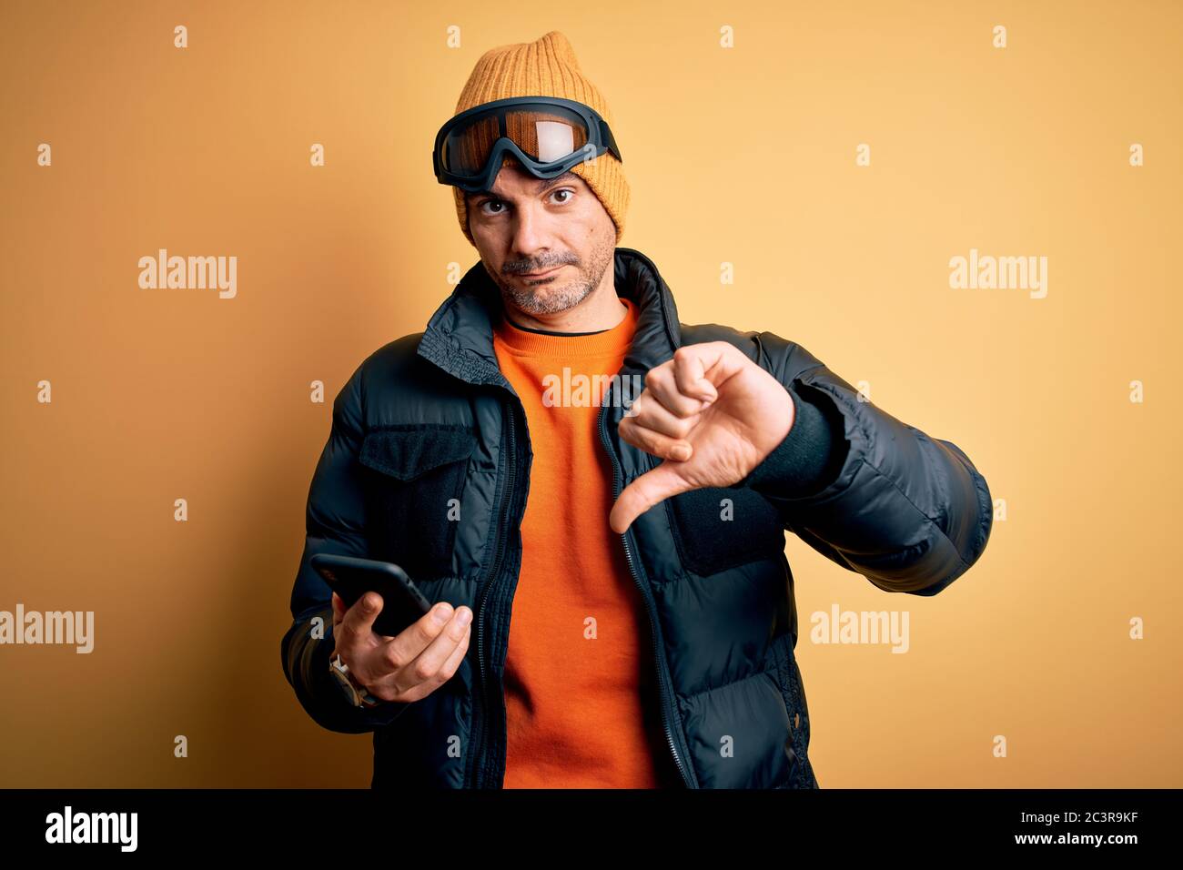 Young handsome skier man wearing ski goggles using smartphone over ...