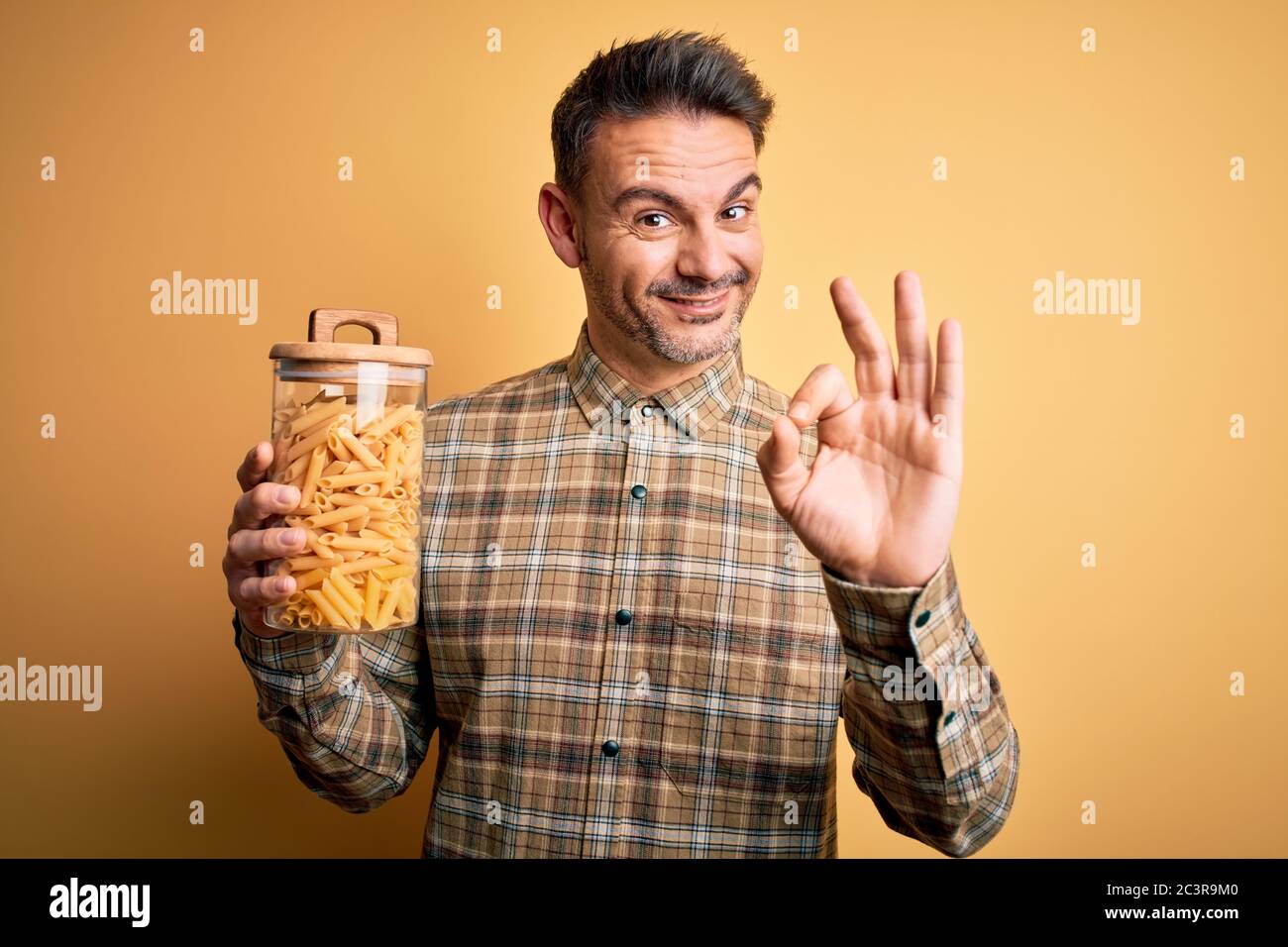 Young handsome man holding jar with dry italian pasta macaroni over ...