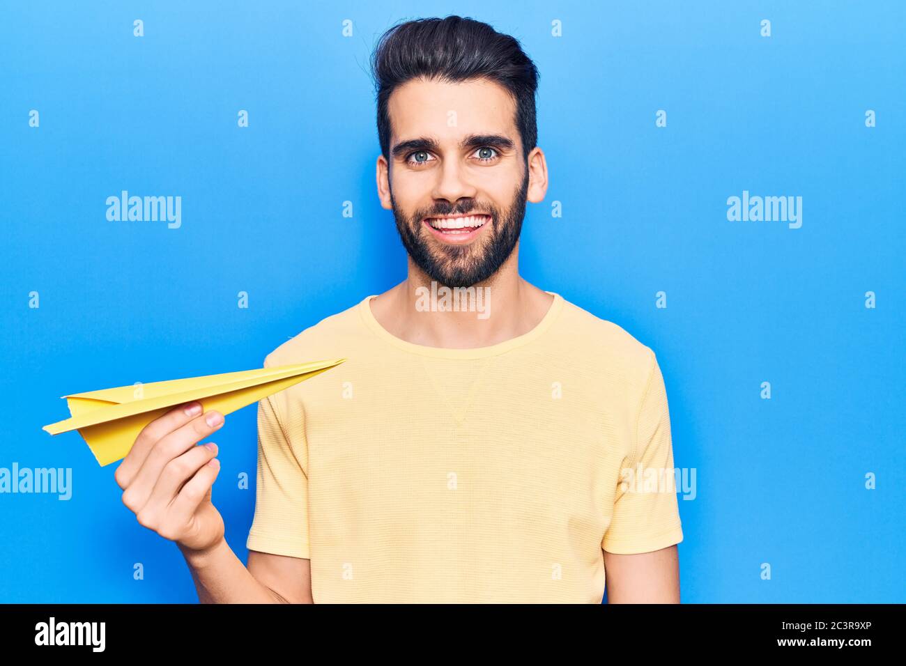 Young handsome man with beard holding yellow paper airplane looking ...