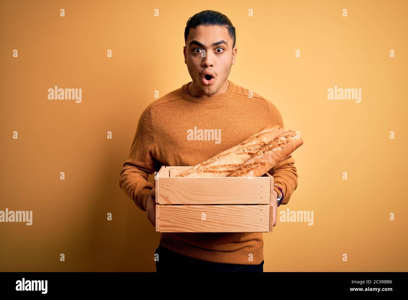 Young baker brazilian man holding box with homemade bread over isolated ...