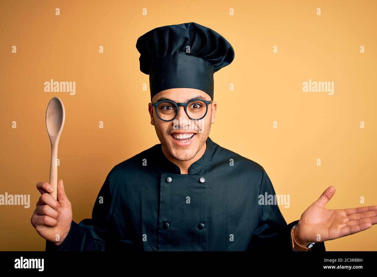 Young brazilian chef man wearing cooker uniform and hat holding wooden ...