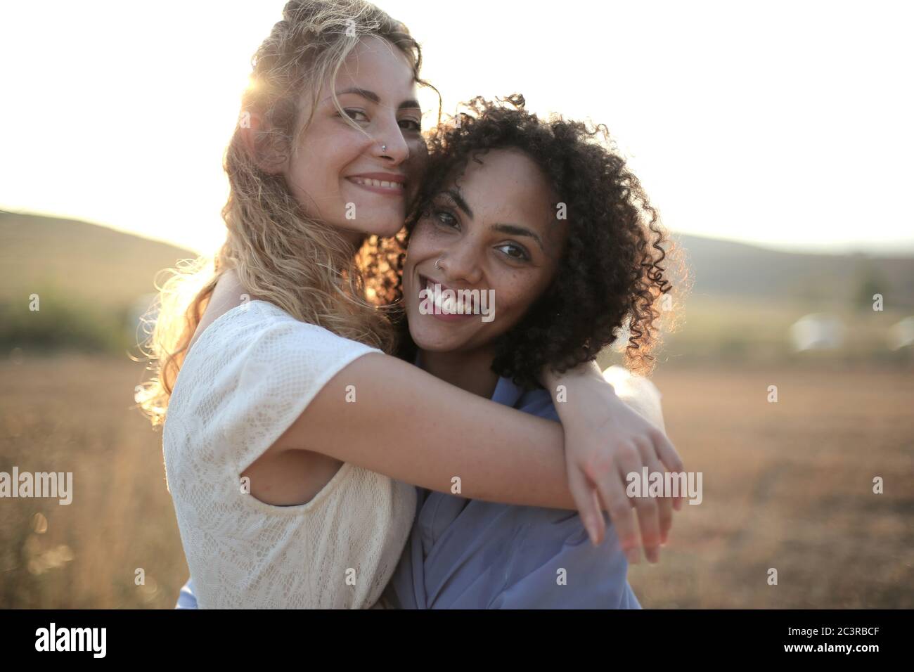 Female friends hugging each other surrounded by a dry field Stock Photo ...