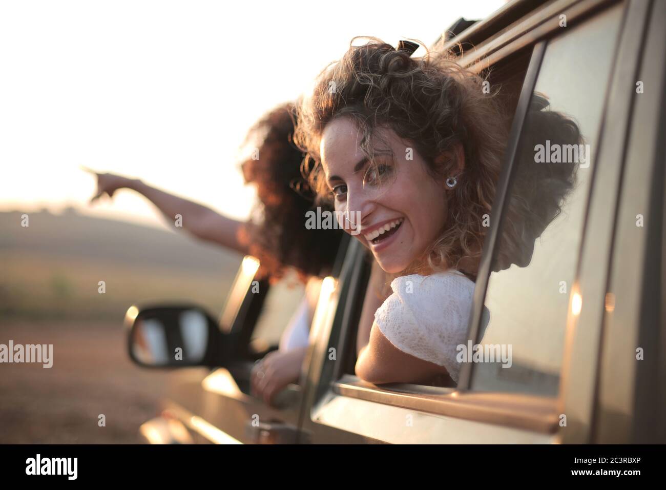 Woman looking back out of the car window behind another one pointing ...