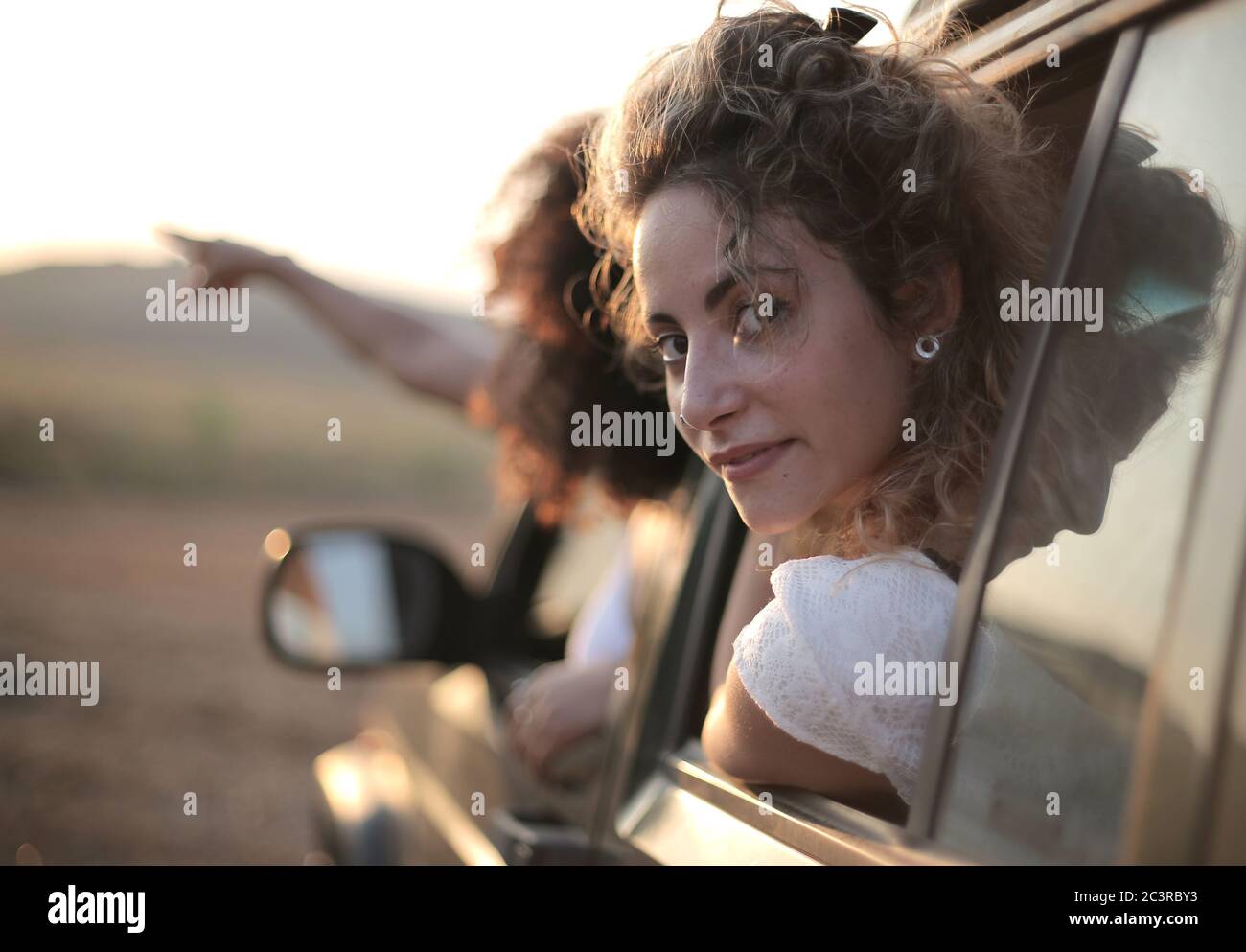 Woman looking back out of the car window behind another one pointing ...