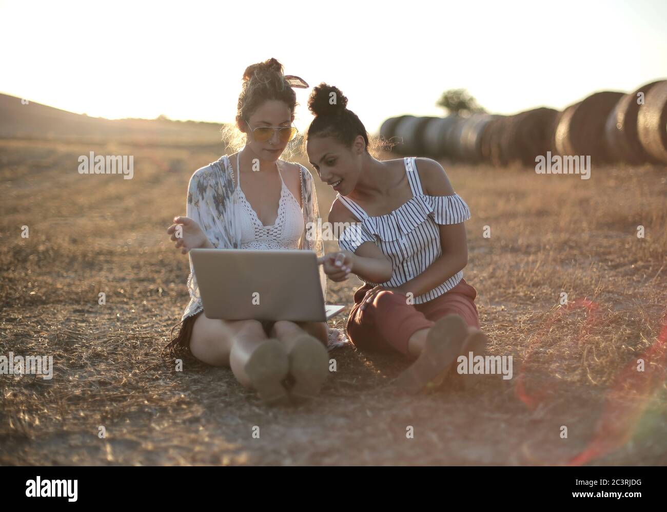 Young females working on the computer sitting on the grass and happily ...