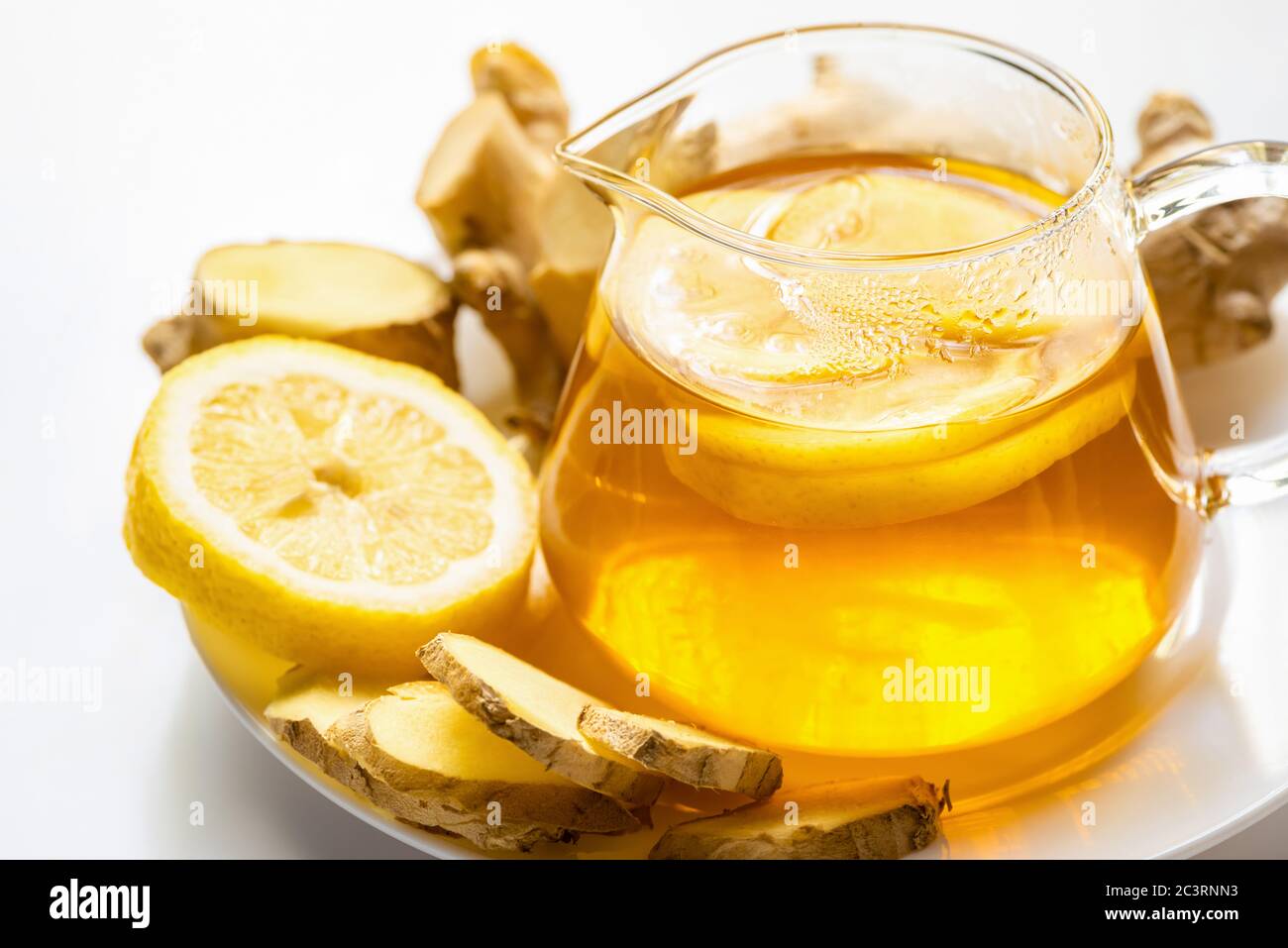 hot tea in teapot near ginger root, lemon on plate on white background ...