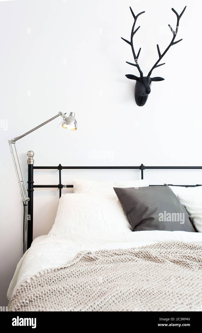 Vertical shot of a bed with white sheets and a deer statue of the wall ...