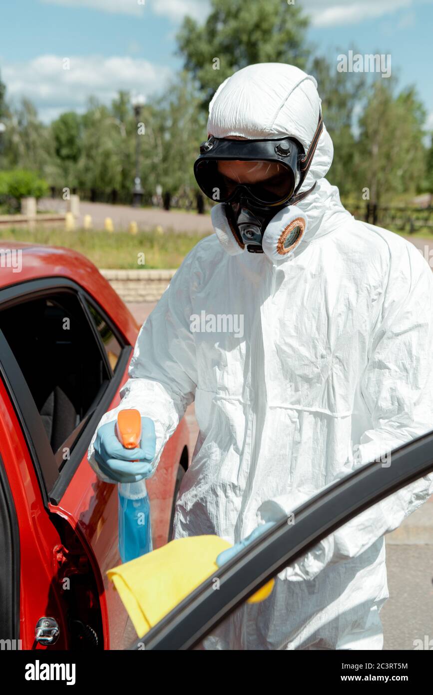 cleaner in hazmat suit cleaning car with antiseptic spray and rag ...