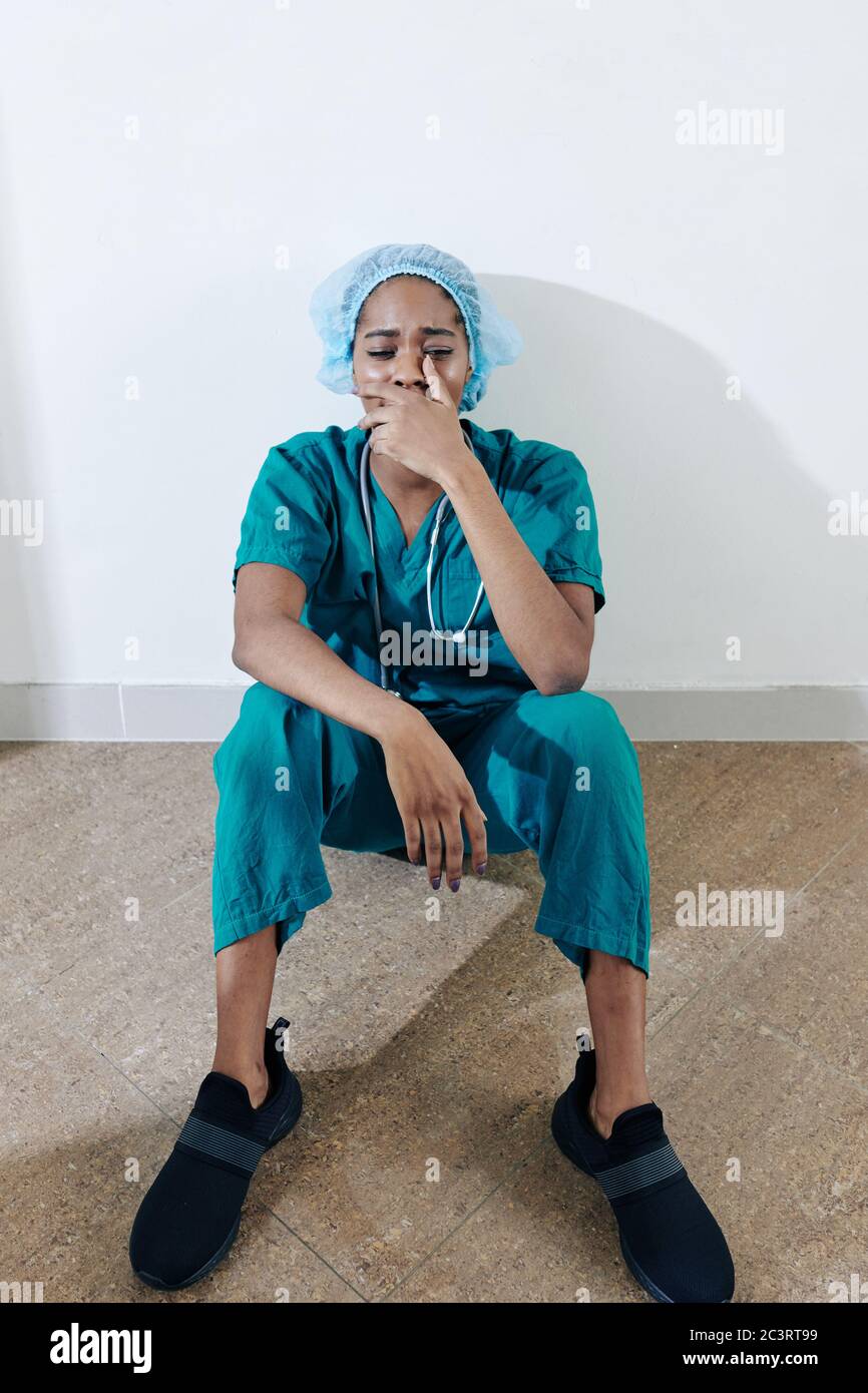 Crying exhausted young nurse sitting on the floor in office corridor ...