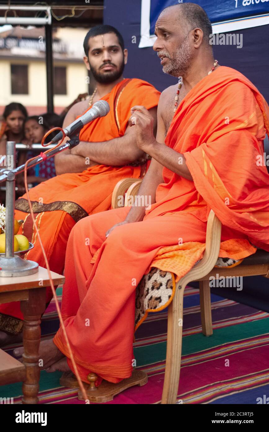 A saffron-clad senior Hindu priest flanked by by a junior priest giving ...