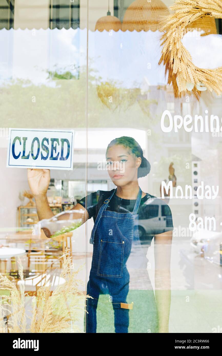 Sad young Black female bakery shop owner sticking closed sign on glass ...