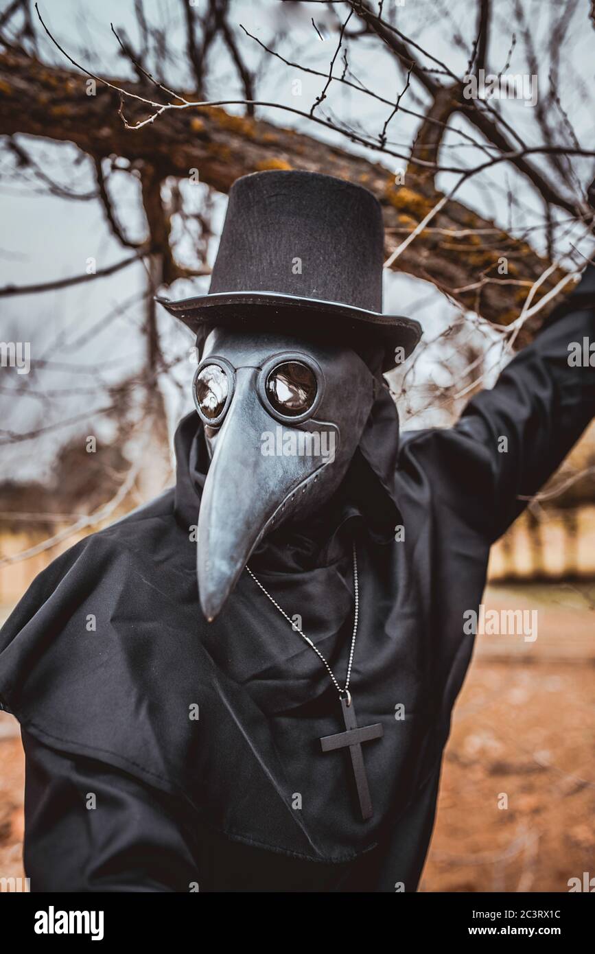 Plague doctor with a cane and a classic dark garb with a cross Stock ...