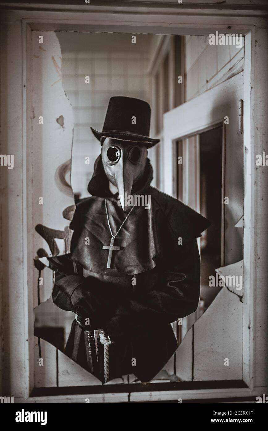 A plague doctor with a cane and a classic dark garb with a cross Stock ...