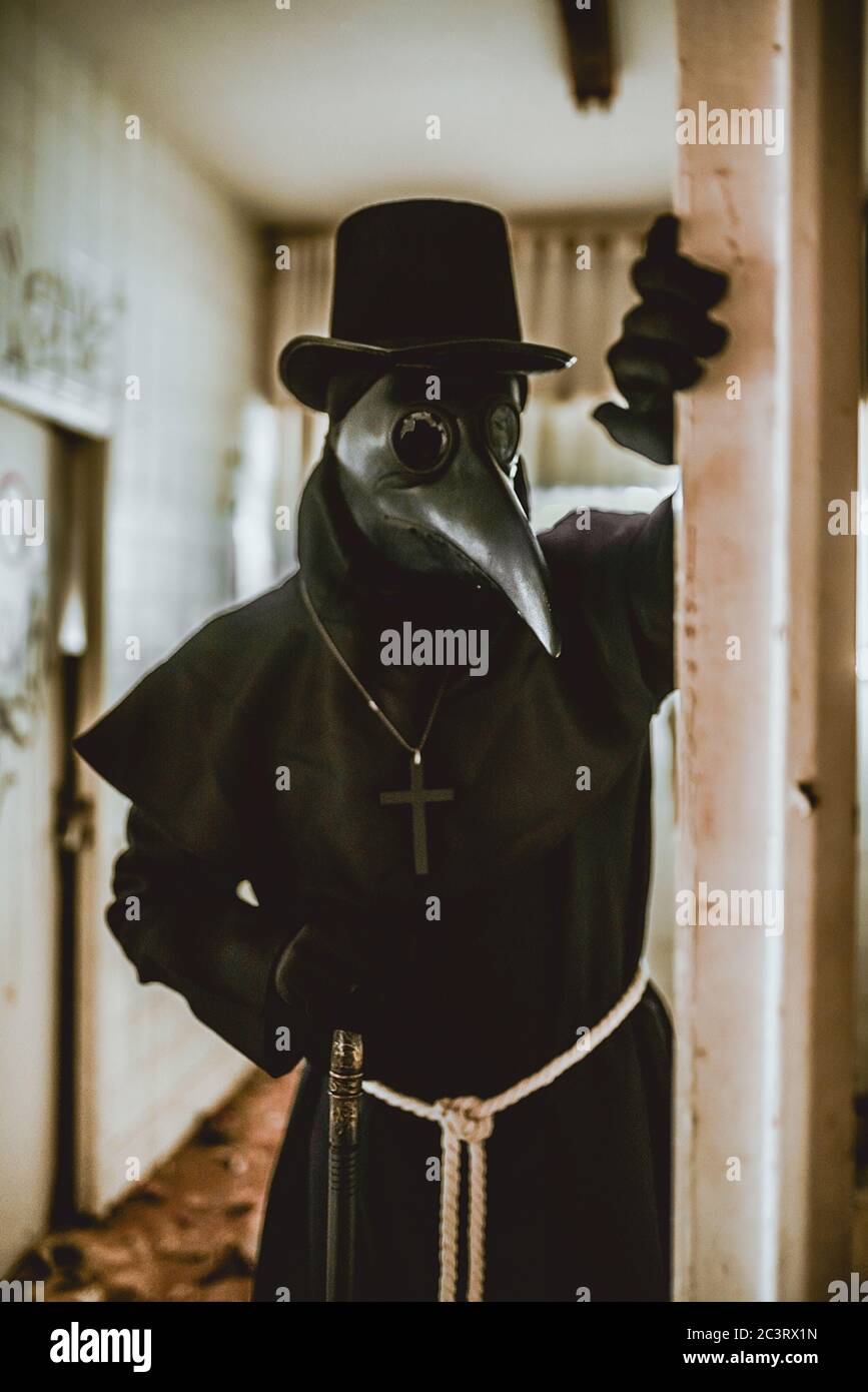 Plague doctor with a cane and a classic dark garb with a cross Stock ...
