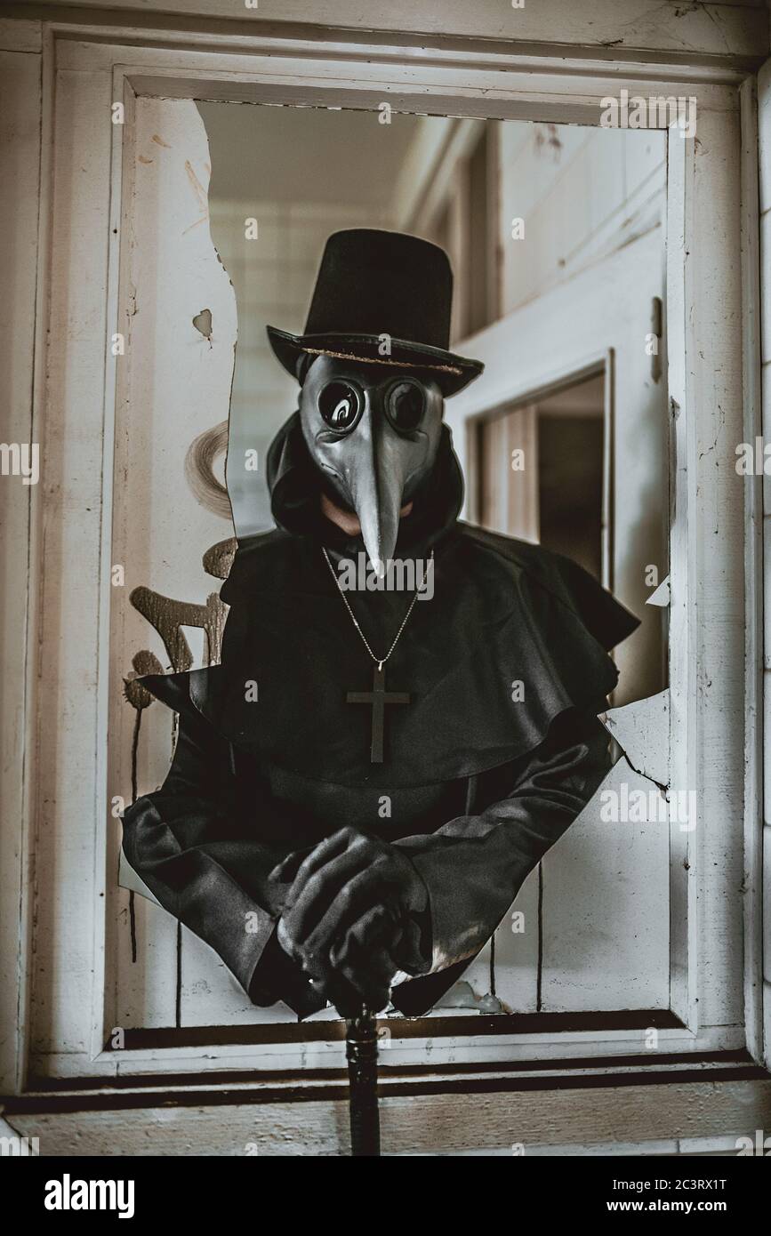 A plague doctor with a cane and a classic dark garb with a cross Stock ...
