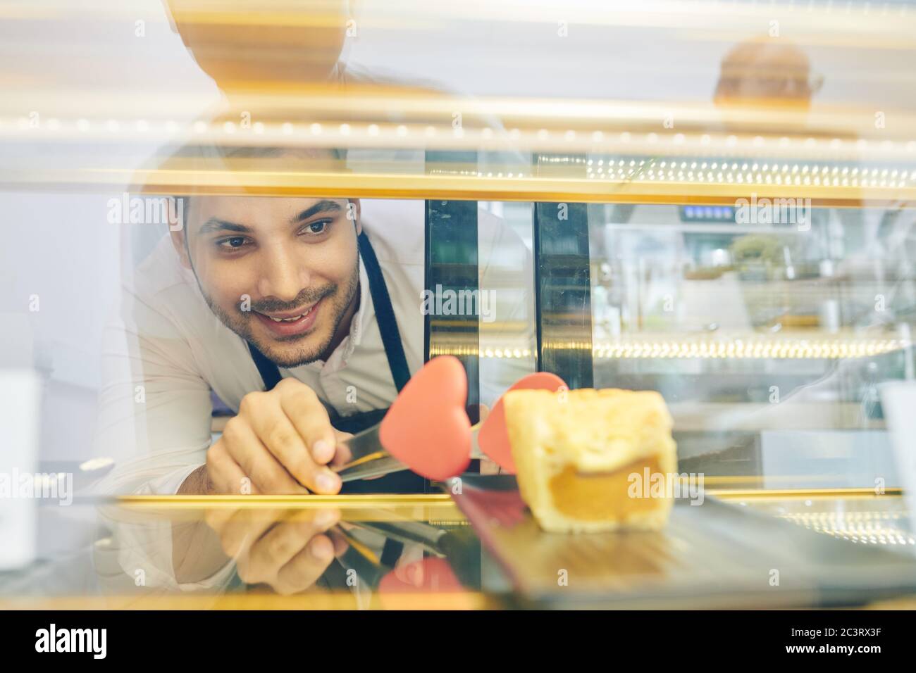 Smiling young bakery shop owner taking last piece of cake from showcase ...