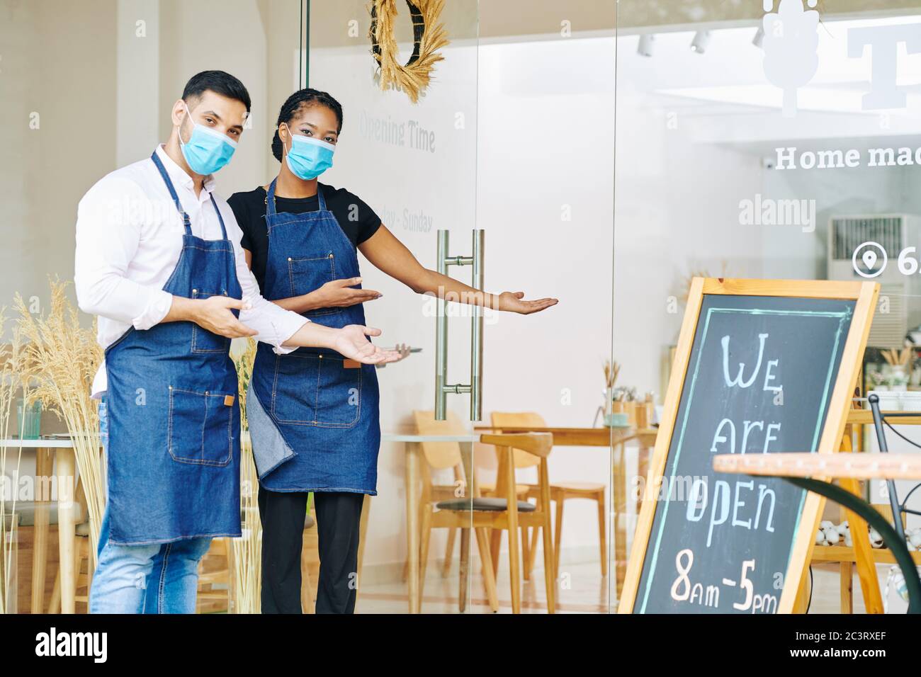 Bakery shop workers in denim aprons and medical masks making welcoming ...