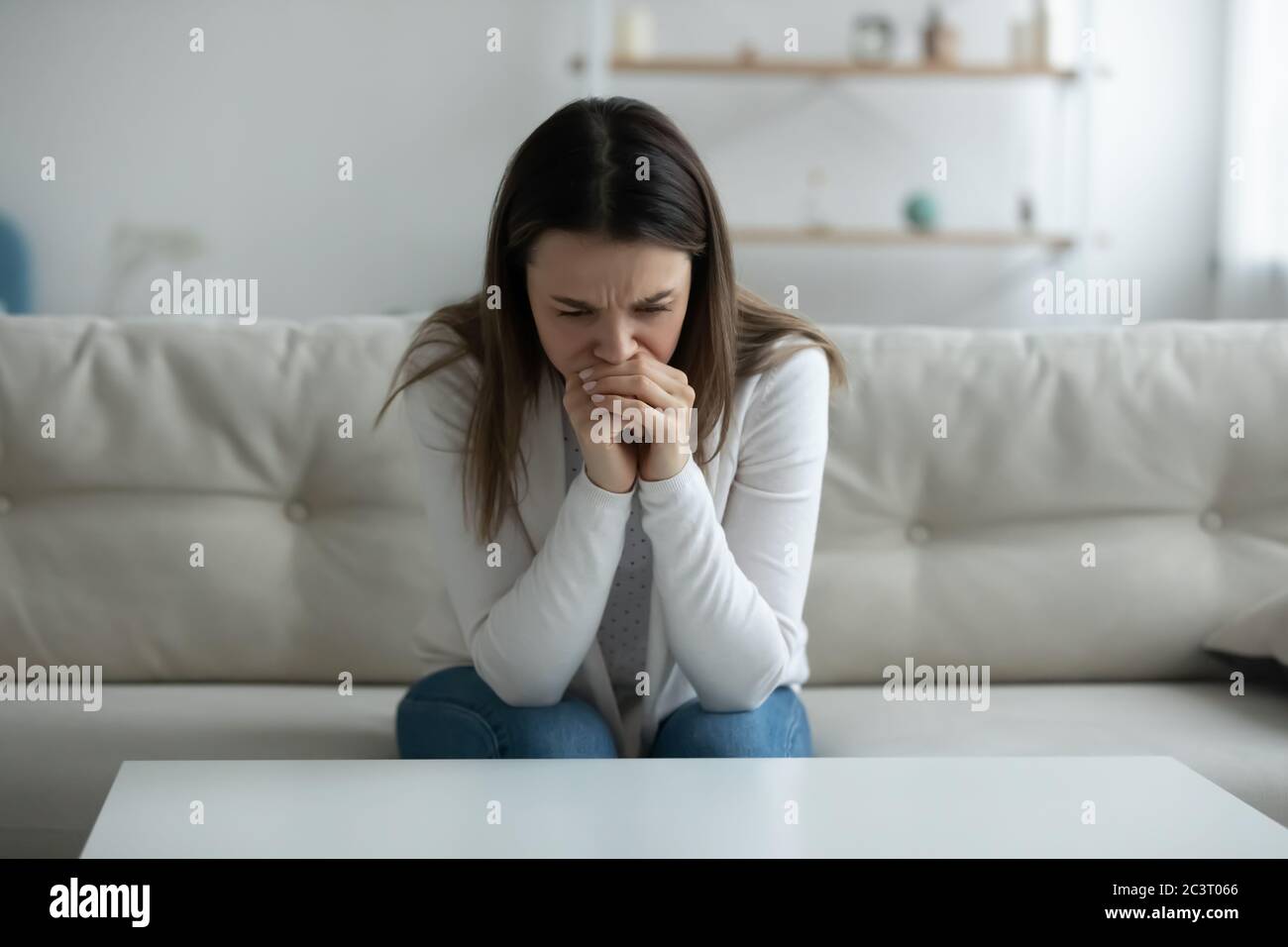 Depressed young woman crying seated on sofa alone at home Stock Photo ...