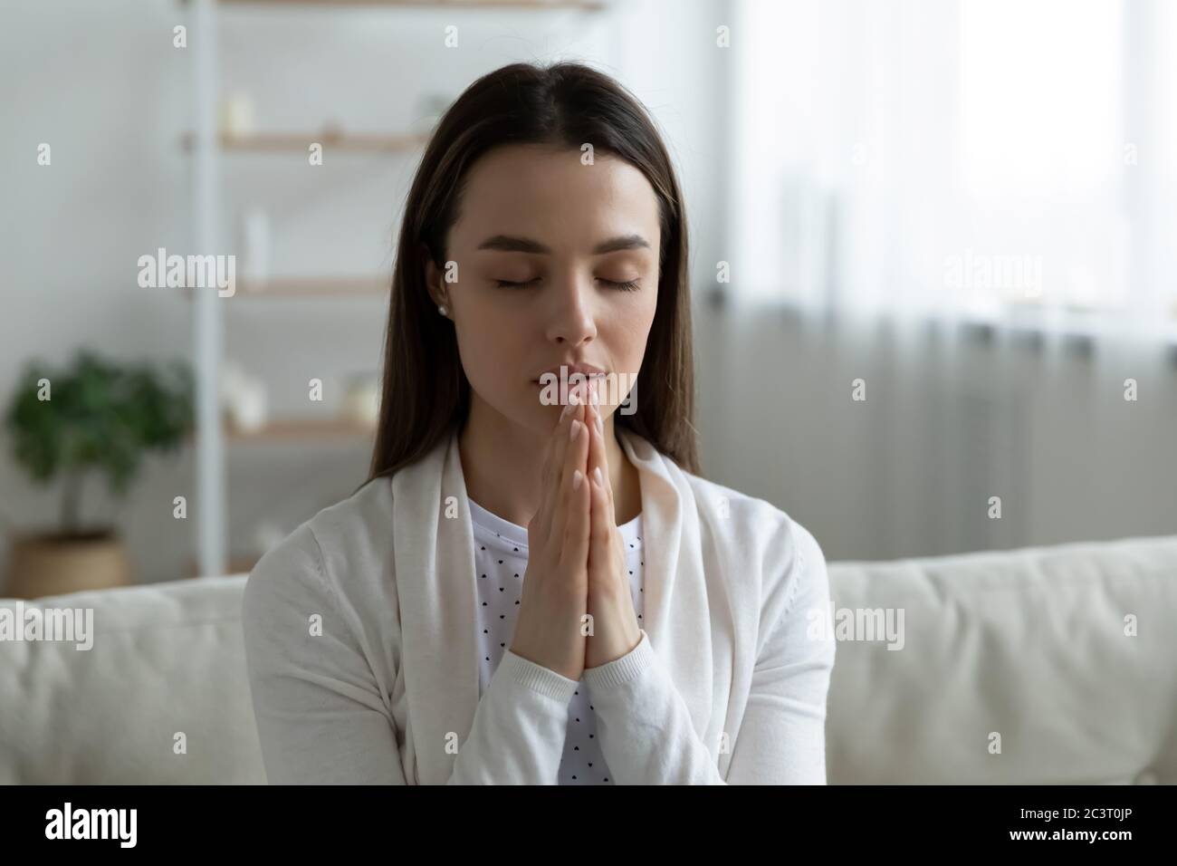 Beautiful young woman praying seated on couch in living room Stock ...
