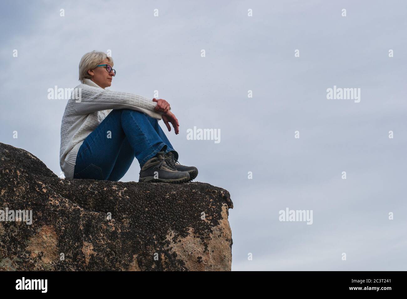 A brooding woman with glasses, dressed in a white sweater and jeans ...