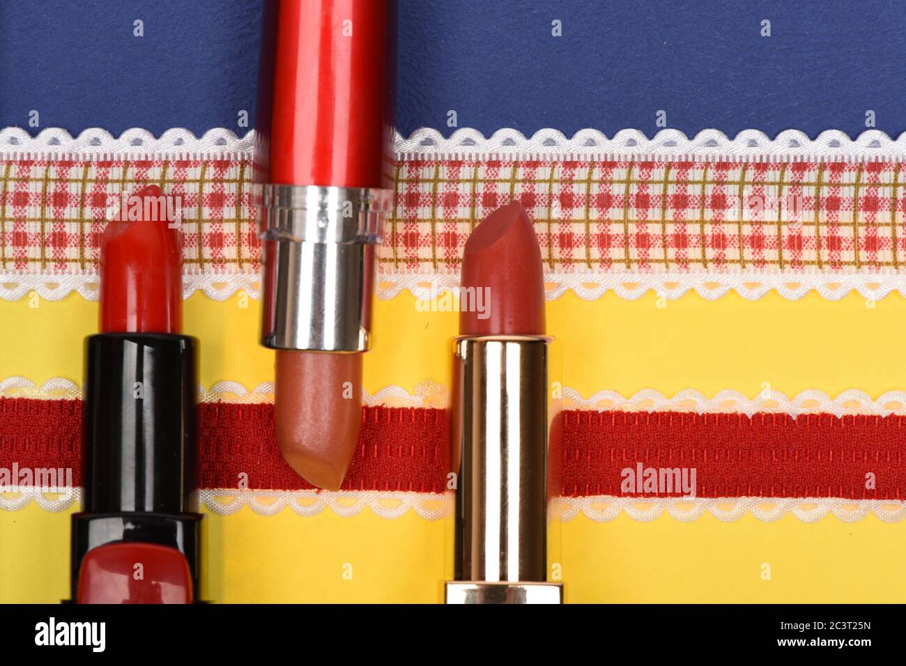Three red, scarlet lipsticks lay on striped background with textile ...