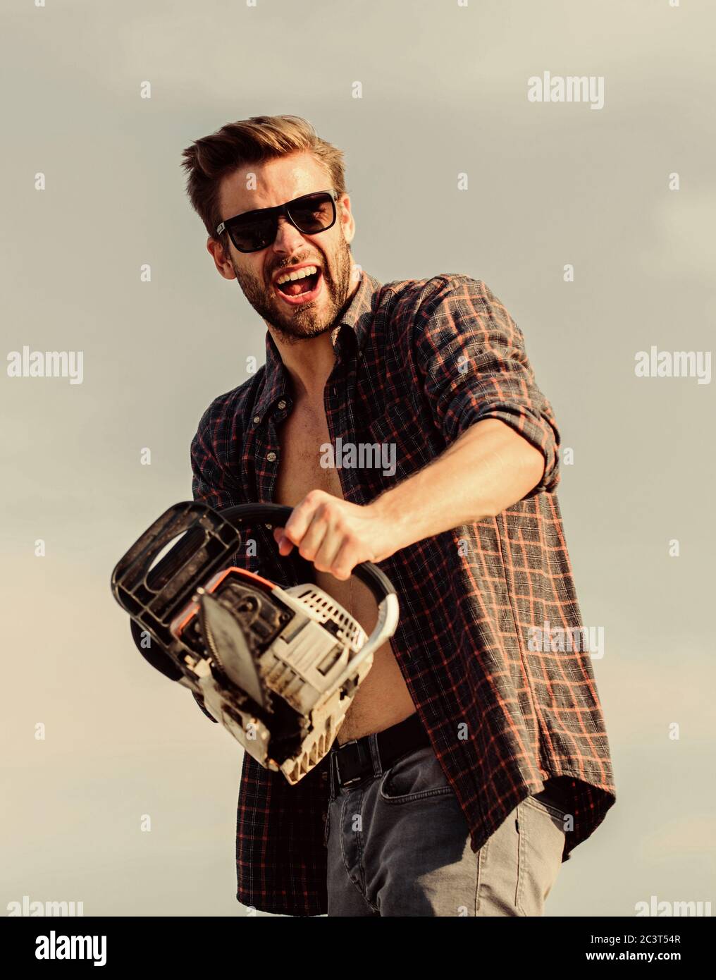 Handsome man with chainsaw blue sky background. Gardener lumberjack ...
