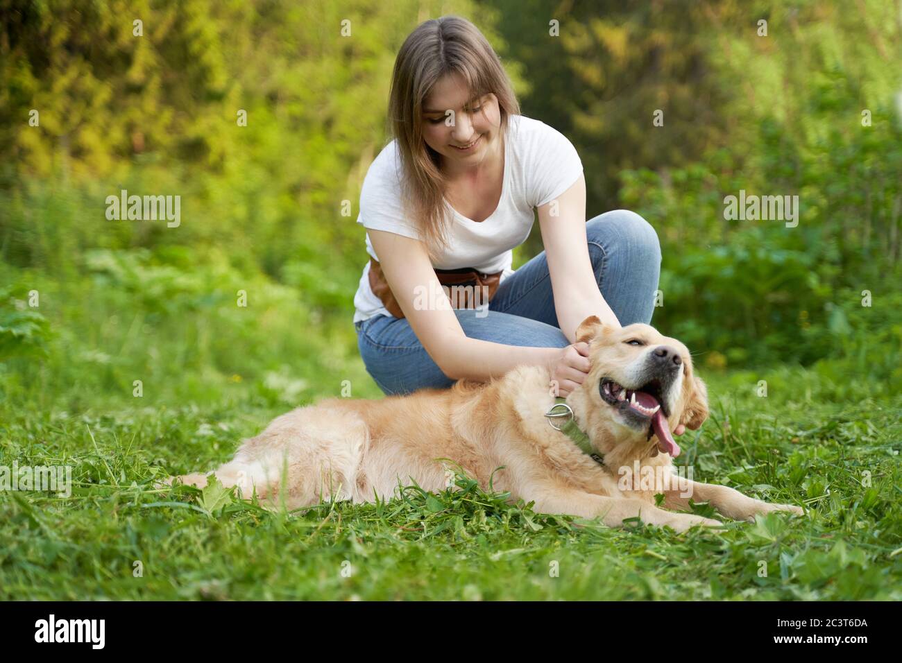 Young woman squatting next to dog while walking Stock Photo - Alamy