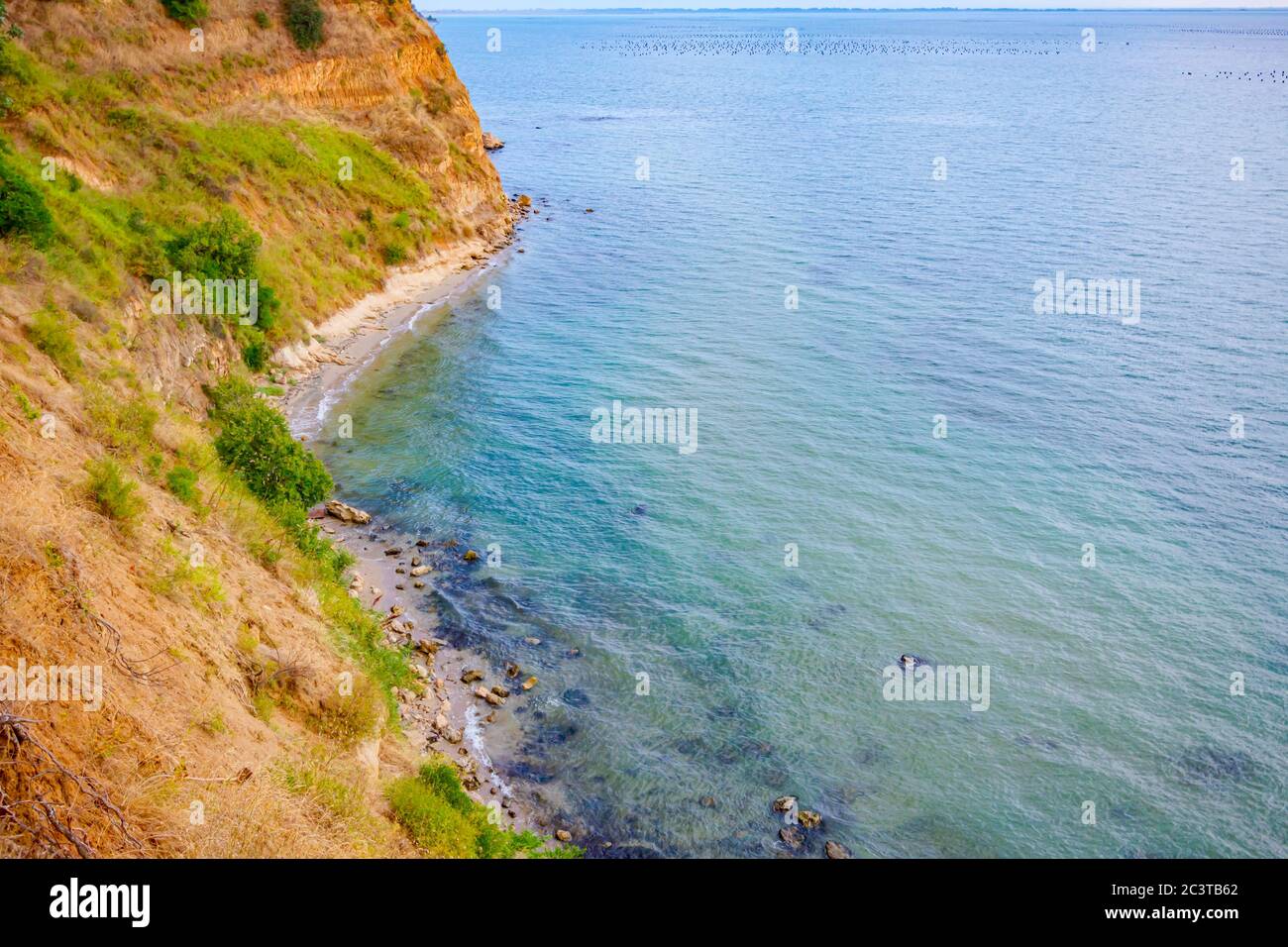 Overgrown cliff with dry grass above sea coastline, along water edge ...