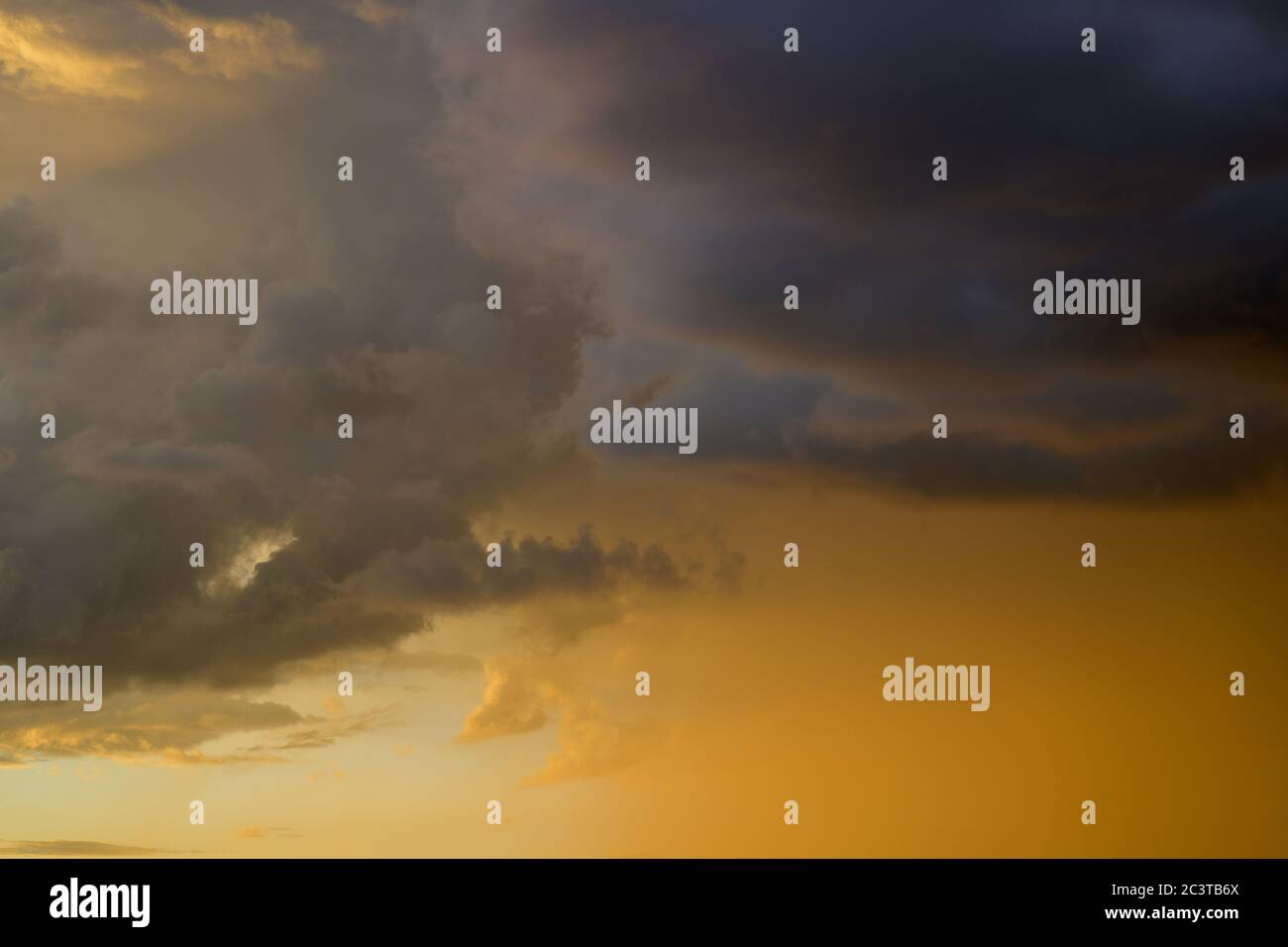 Threatening grey storm clouds in a diffuse colorful orange sunset sky ...