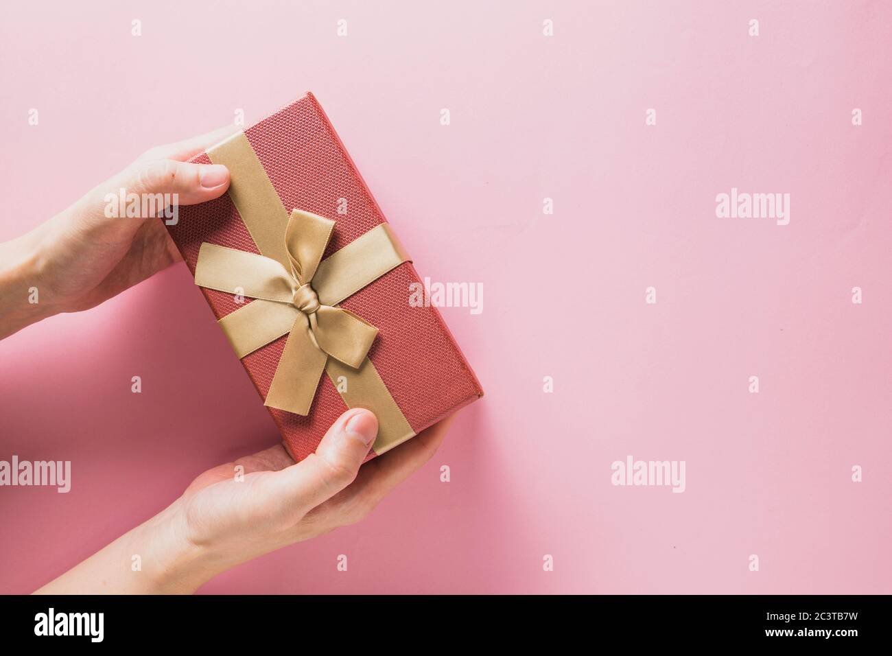 Top view of female hands holding a box with gift on pink background ...