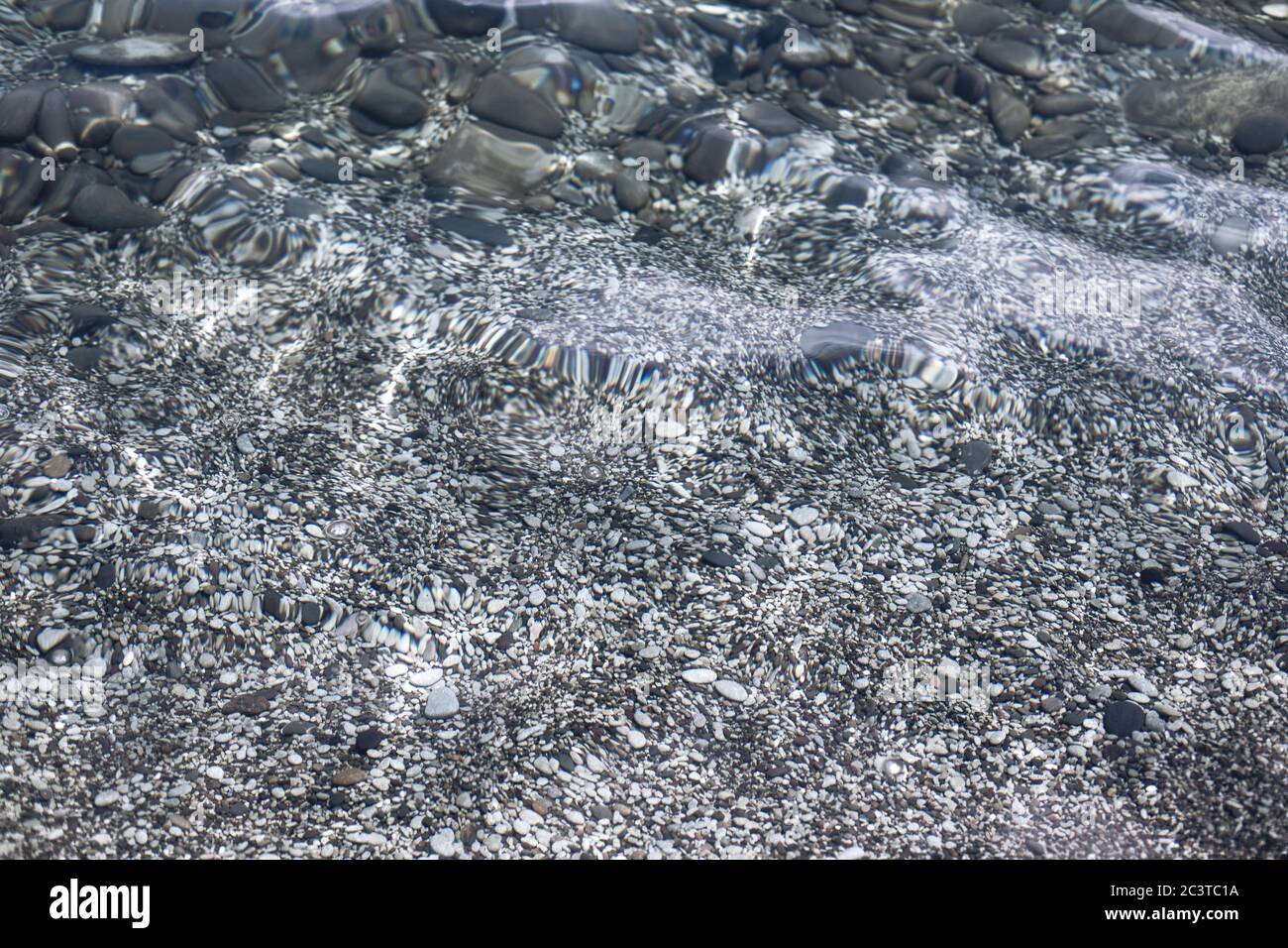transparent clear calm water surface with small grey pebbles sea bottom ...