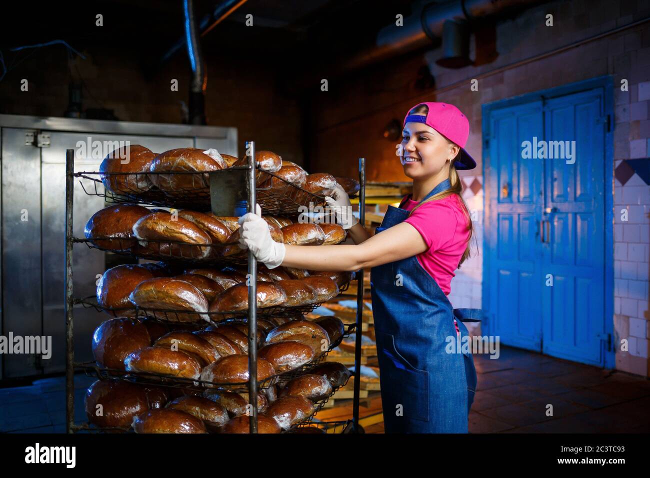 A baker girl takes hot bread in a bakery against the background of ...
