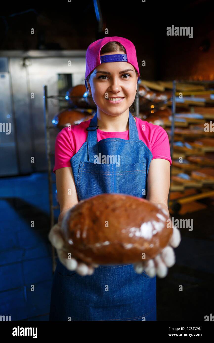 A baker girl takes hot bread in a bakery against the background of ...