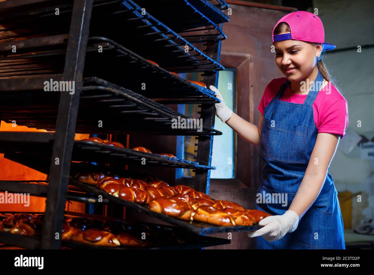 Young girl baker holds a tray with hot pastries against the background ...