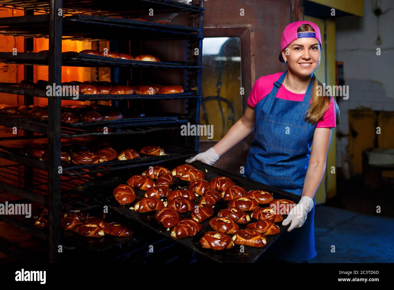Girl baker holds a tray with hot pastries in the bakery. Production of ...