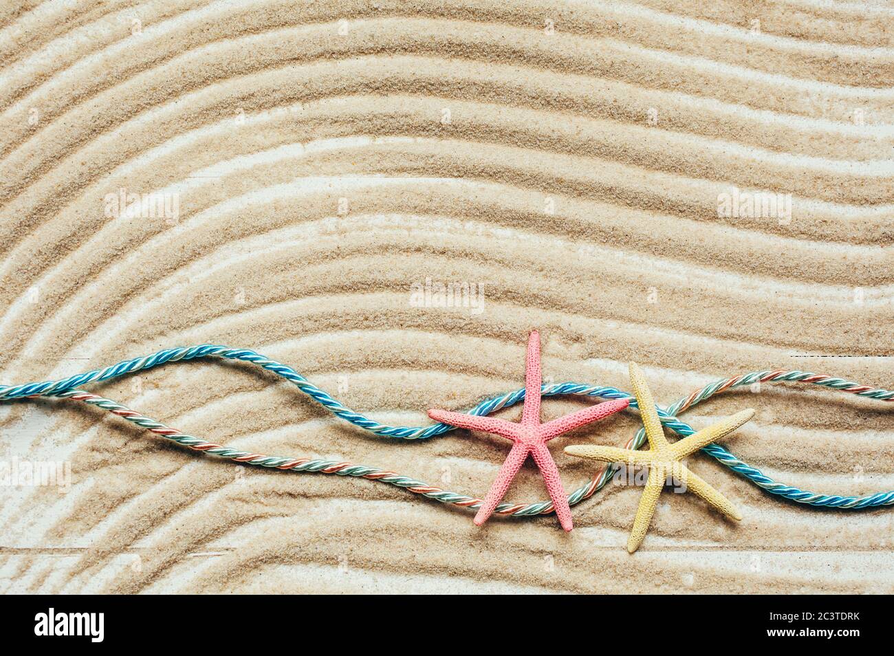 Two colored starfish and two colored marine ropes on textured wavy sand ...