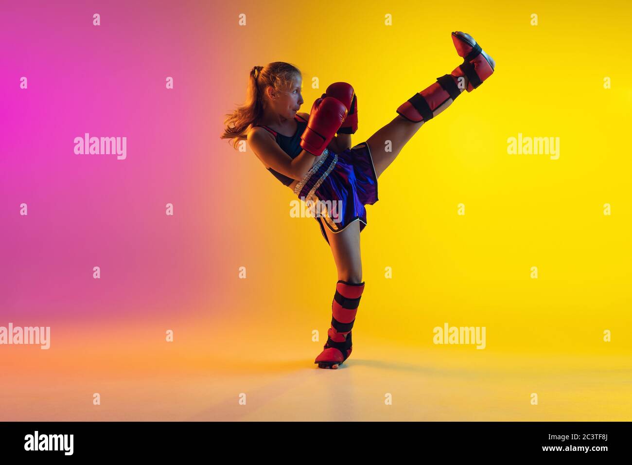 Little caucasian girl, kick boxer on gradient background in neon light ...