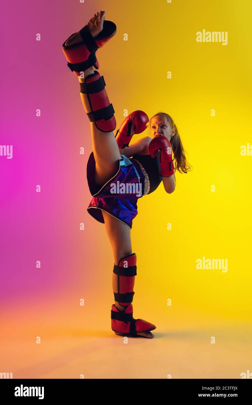 Little caucasian girl, kick boxer on gradient background in neon light ...