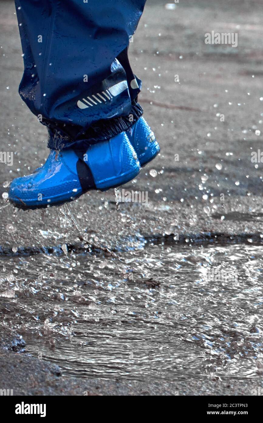 Happy child jumping in puddle in waterproof coat. A boy have fun in the ...