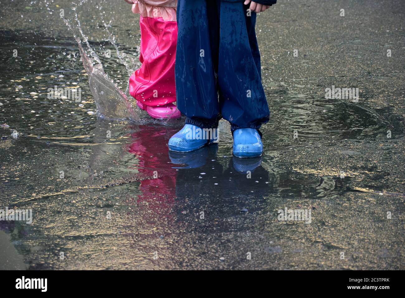 Happy children jumping in puddle in waterproof coat. Boy and girl have ...
