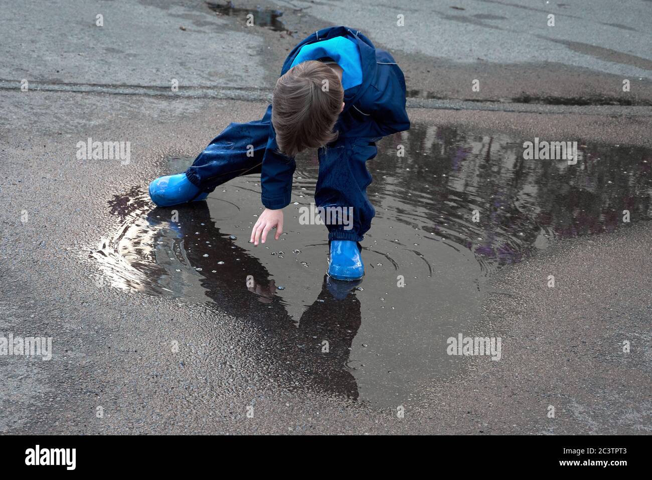 Happy child jumping in puddle in waterproof coat. A boy have fun in the ...