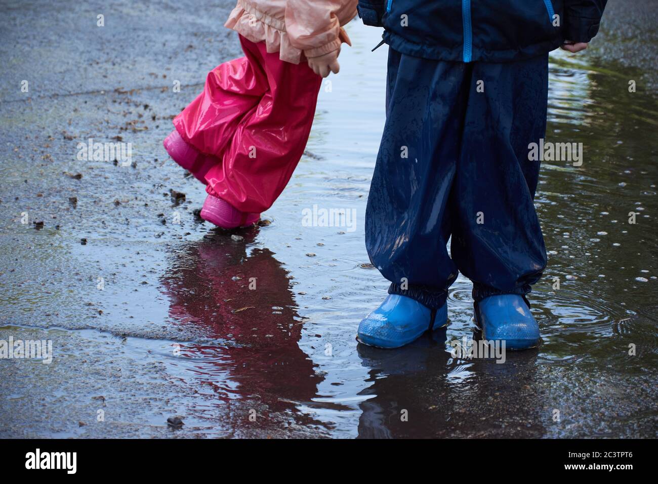 Happy children jumping in puddle in waterproof coat. Boy and girl have ...