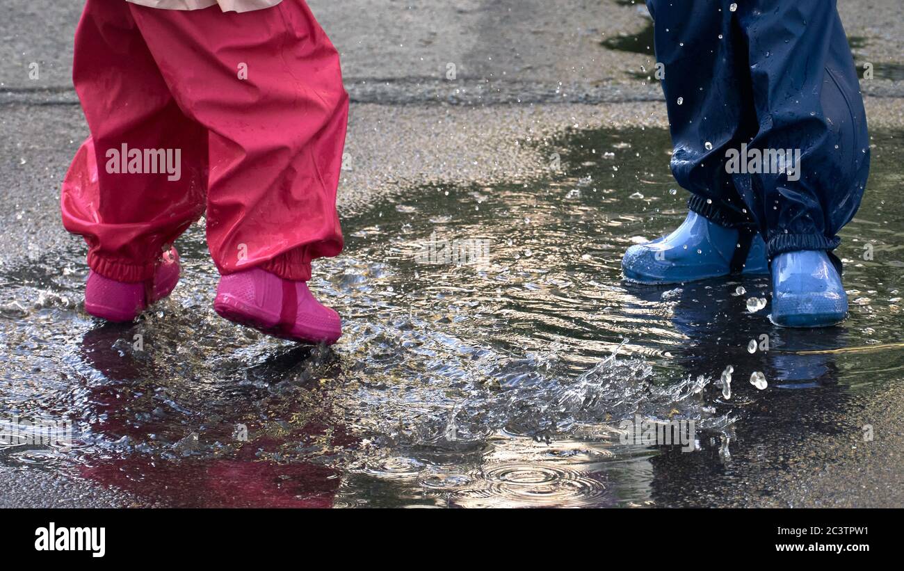 Happy children jumping in puddle in waterproof coat. Boy and girl have ...