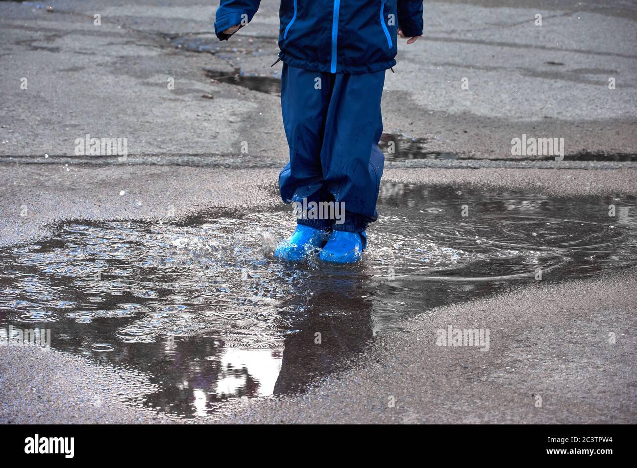 Happy child jumping in puddle in waterproof coat. A boy have fun in the ...